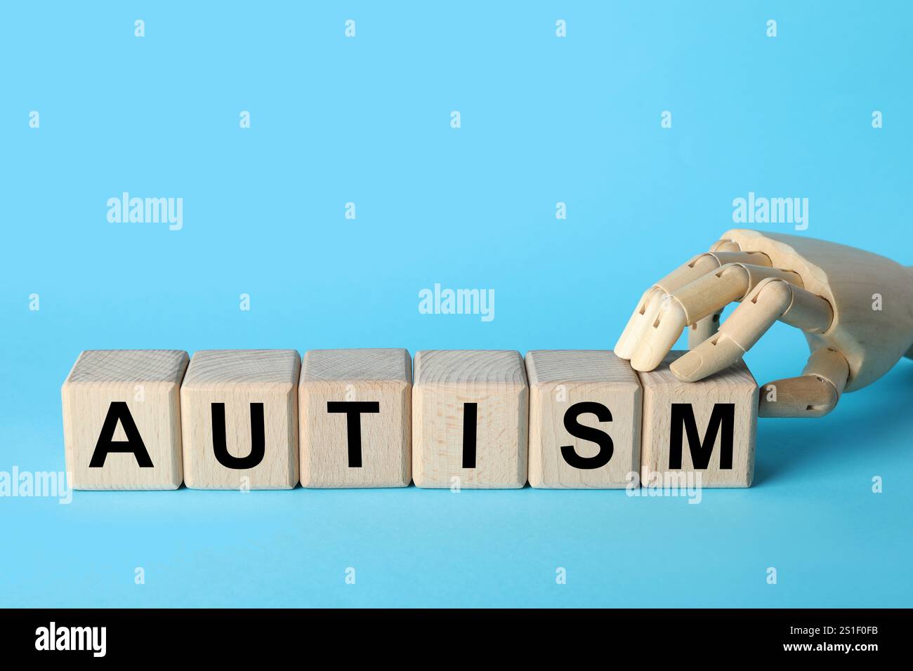 Word Autism made of wooden cubes and mannequin hand on light blue ...