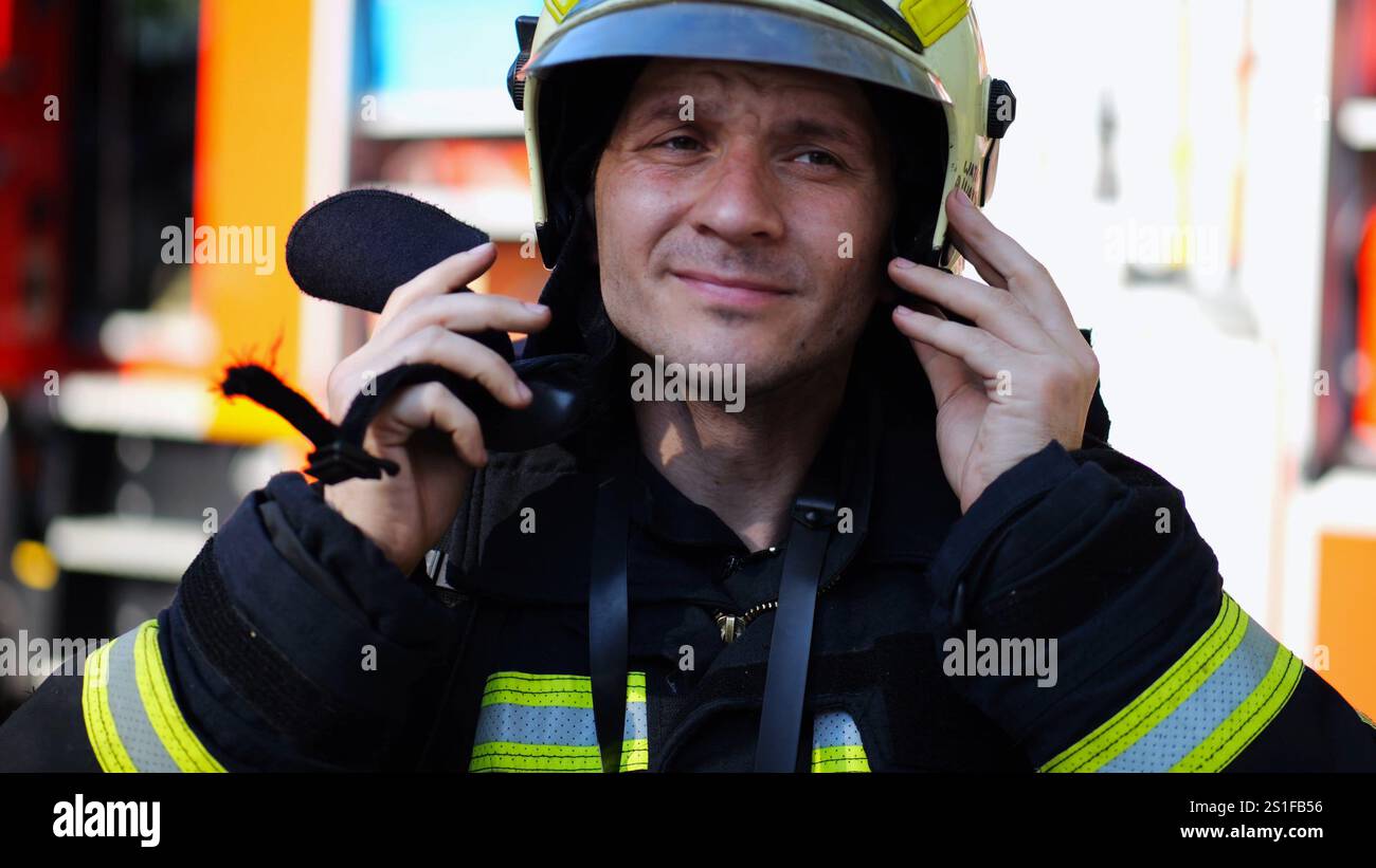Young fireguard in protective uniform putting helmet against background ...