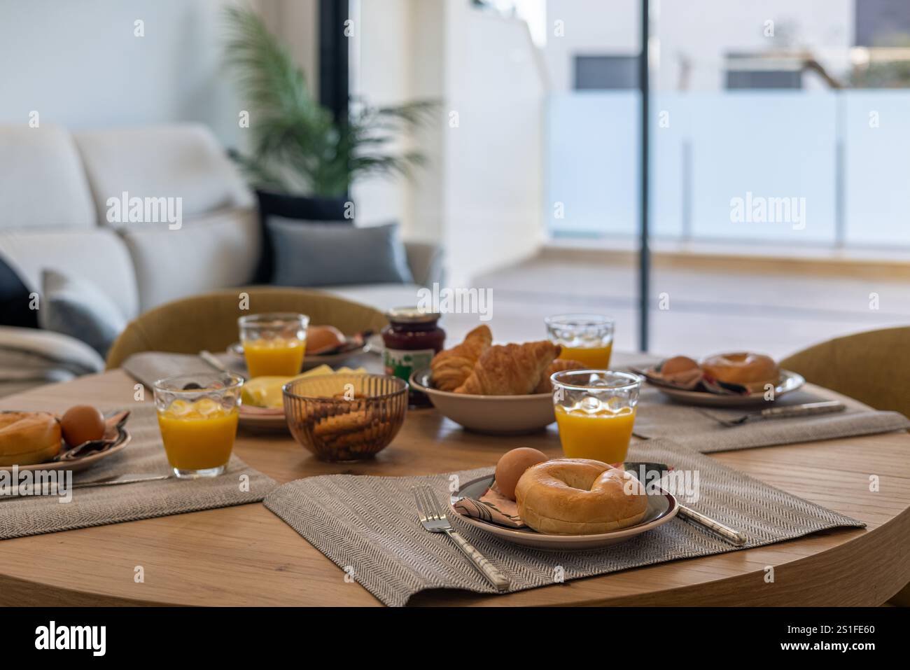 A neatly set breakfast table with bagels, croissants, eggs, orange ...