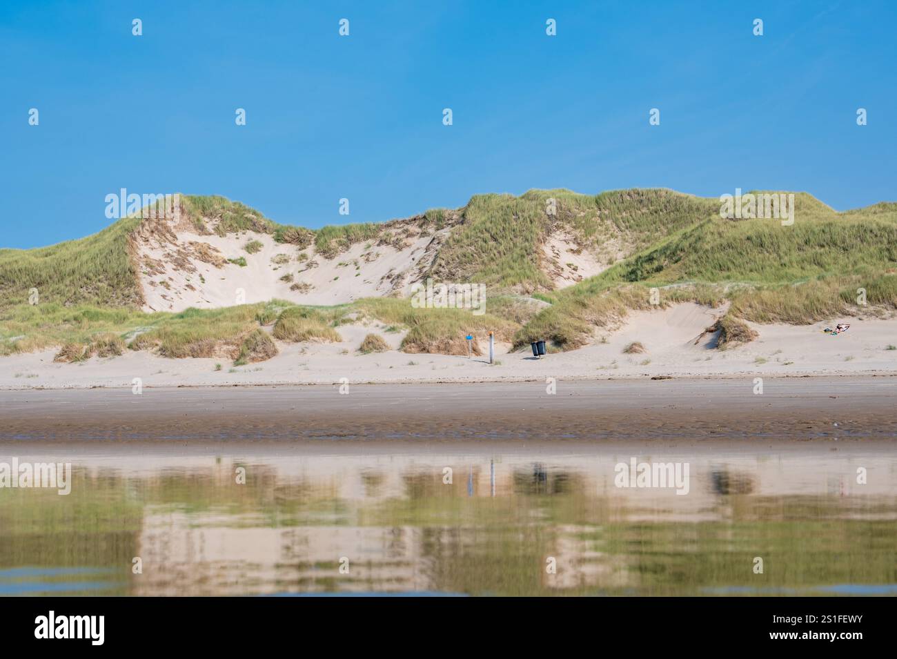 Sand dunes are reflected in the still, standing water at low tide at ...