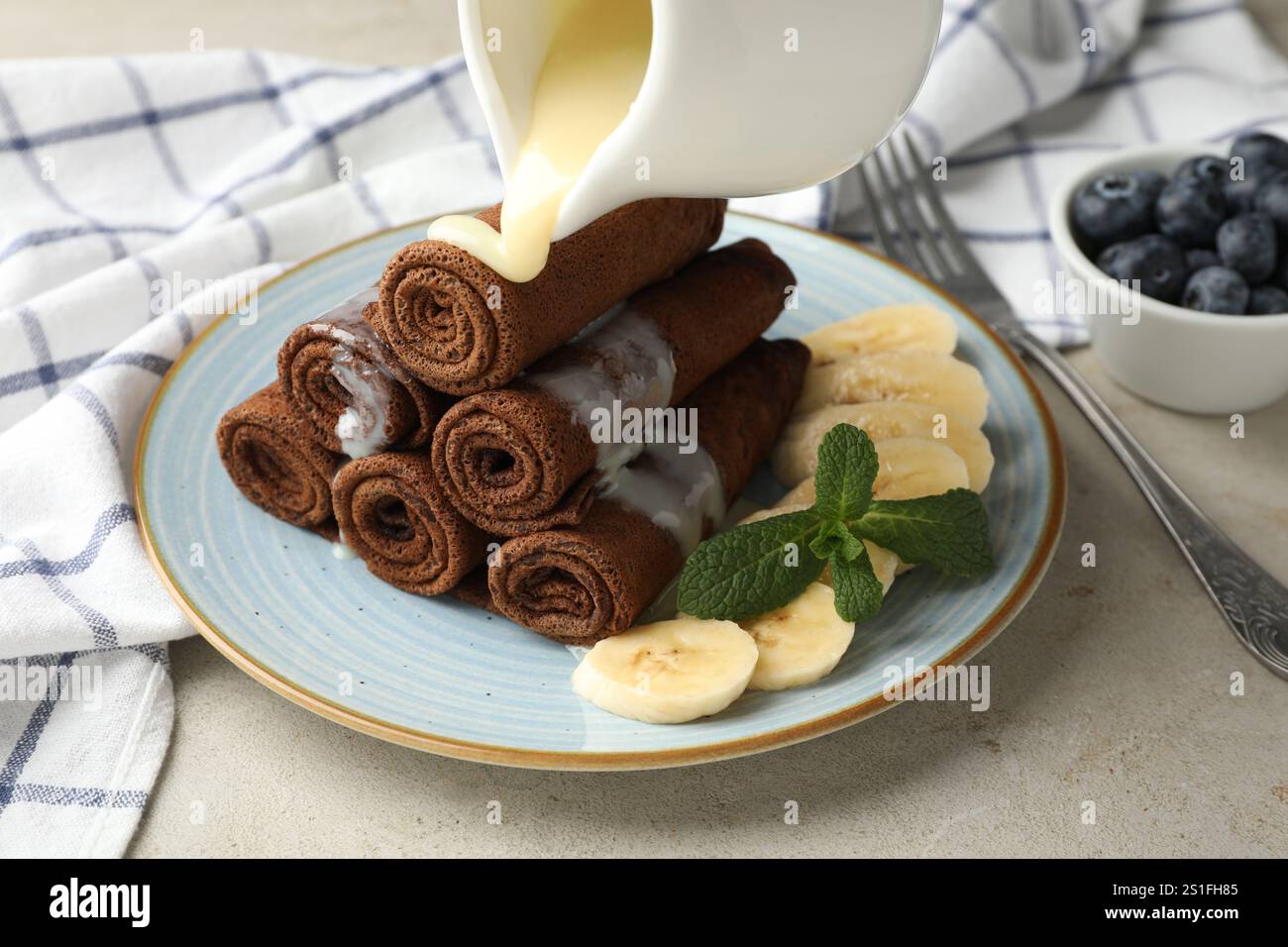 Pouring condensed milk onto chocolate crepes with banana on light table ...