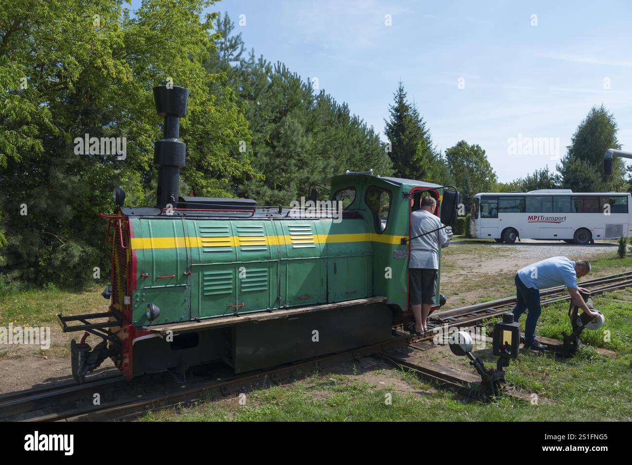 Two people working on a train next to a bus in a green environment ...