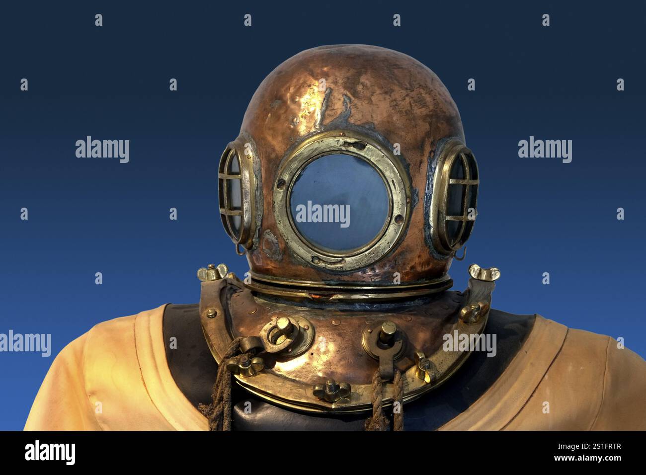 Metal diving helmet with round viewing windows against a blue ...
