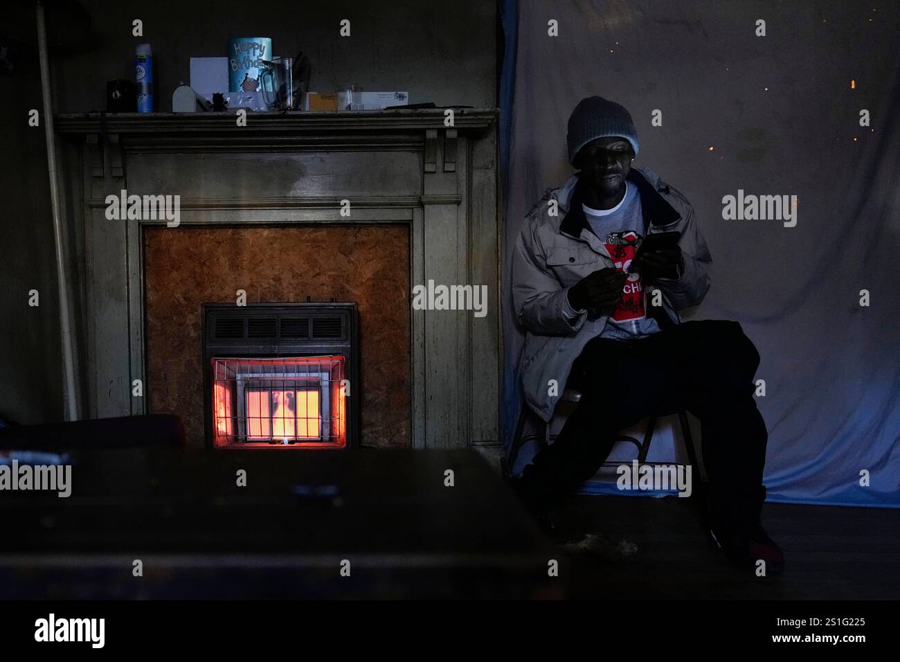 Tyrone Heard looks at his cell phone next to a space heater in his living room, Friday, Dec. 6 ...