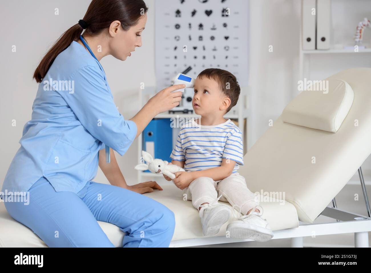 Female pediatrician with infrared thermometer measuring little boy's ...