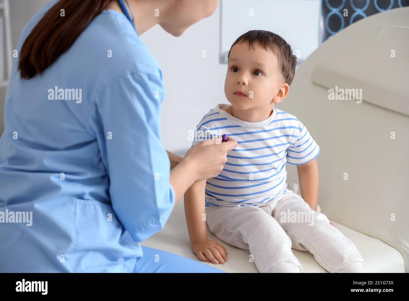 Female pediatrician with cute little boy measuring temperature on couch ...