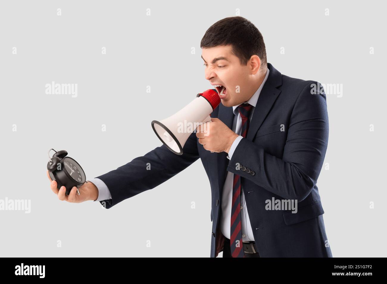 Young businessman with alarm clock shouting into megaphone on light ...