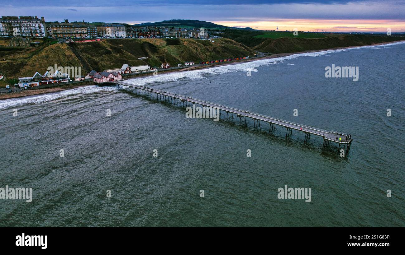 Aerial view of a long pier extending from a coastal town into a dark ...