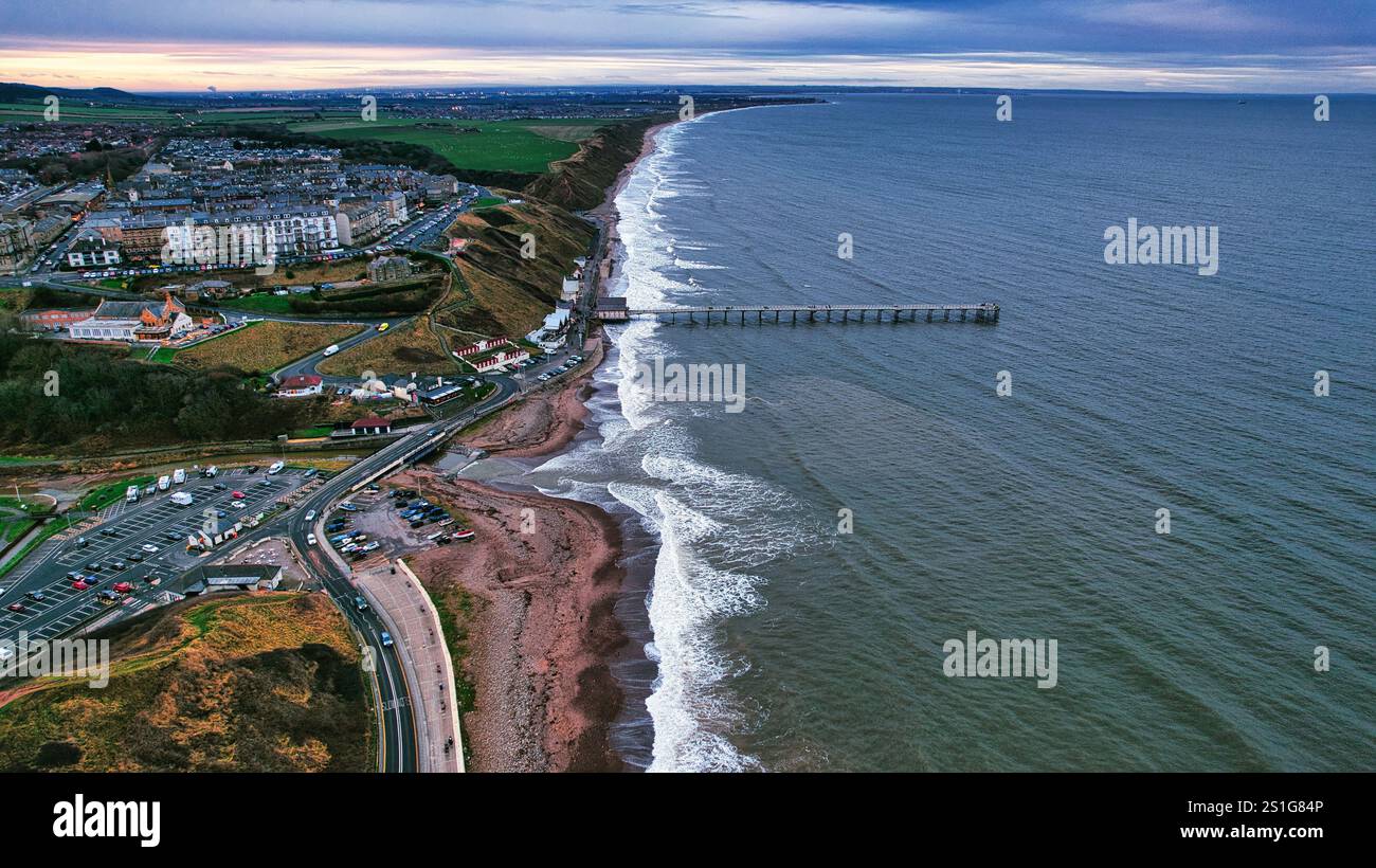 Aerial view of a coastal town, featuring a long pier extending into the ...
