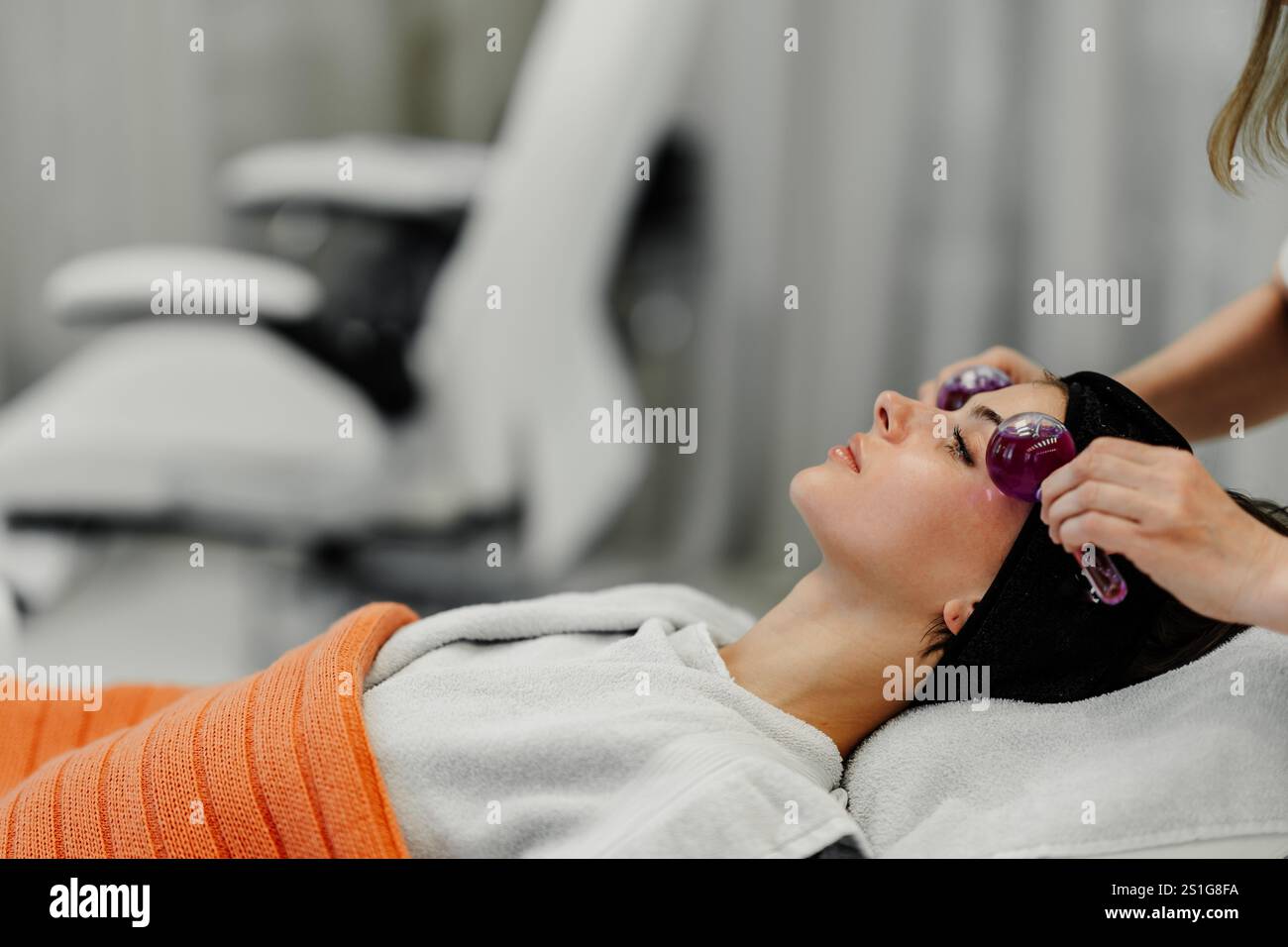 A woman relaxes while getting a facial treatment with roller tools at a ...