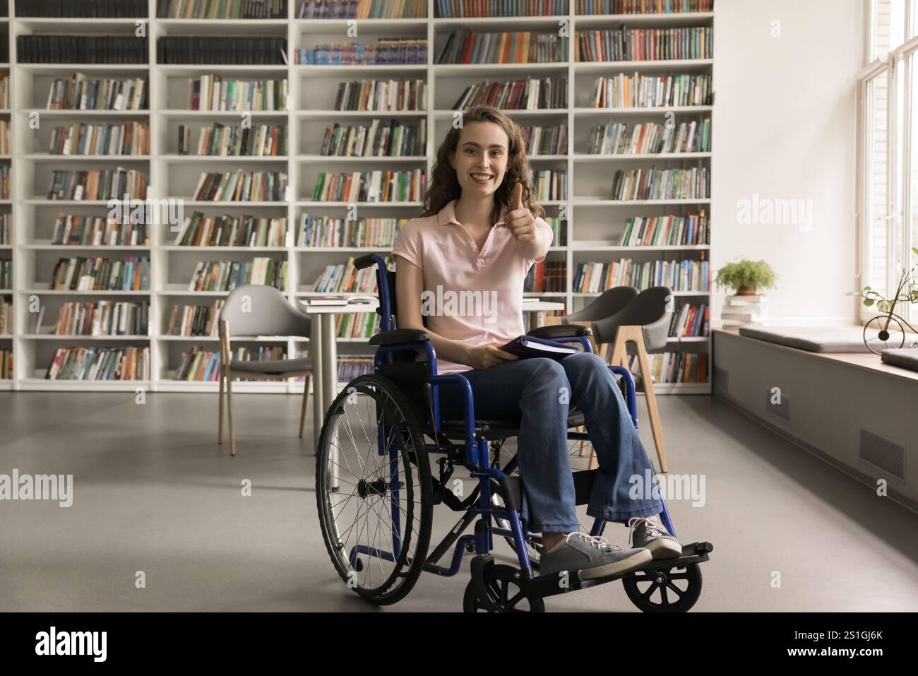 Happy female student using wheelchair show thumb up in library Stock ...