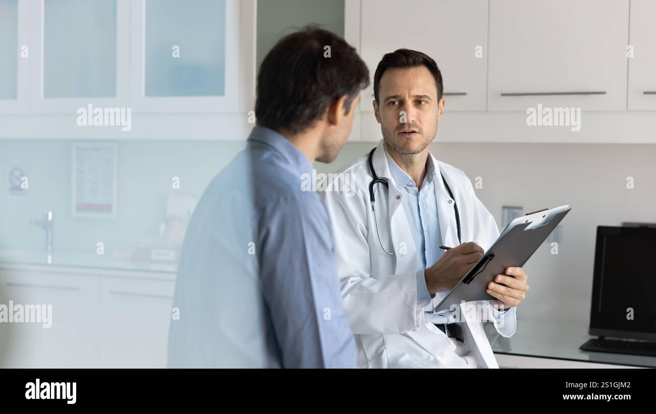Serious doctor giving consultation to male patient, filling up survey ...