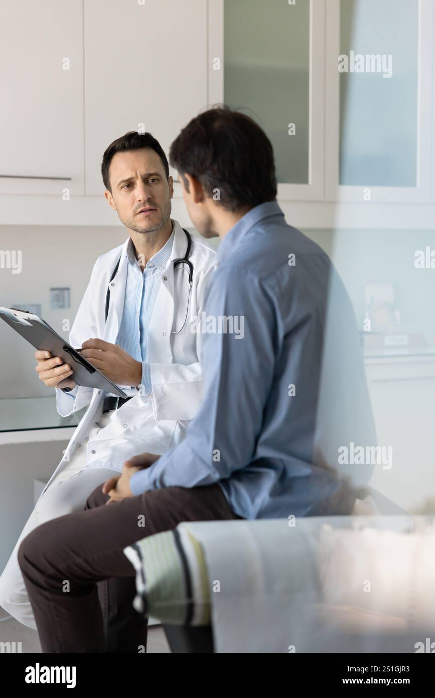 Focused concerned doctor examining male patient, working in clinic ...