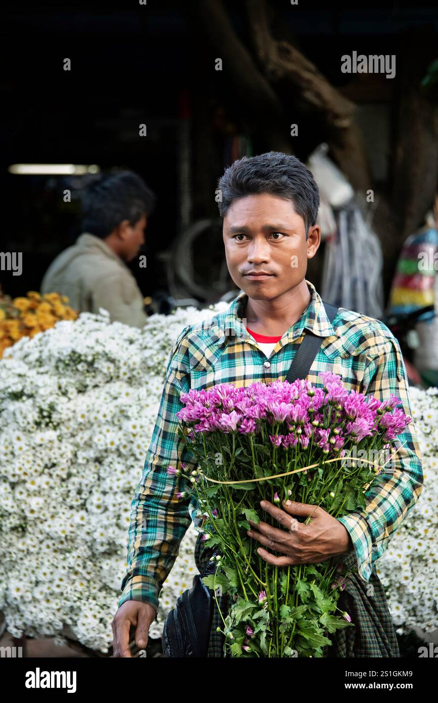 Man carrying a bunch of purple flowers at a flower market in Mandalay ...