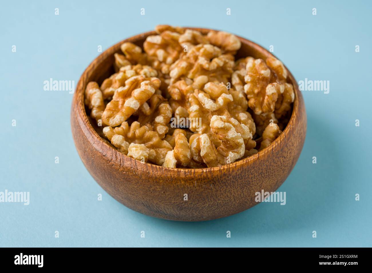 Top view of heap of walnut kernels in wooden bowl on blue background ...
