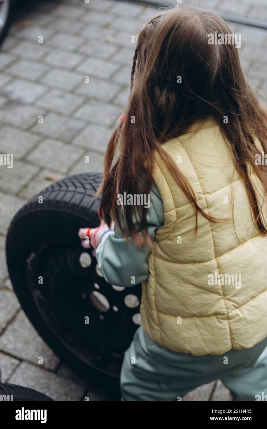 A little girl assists her father in changing the car tires,creating ...