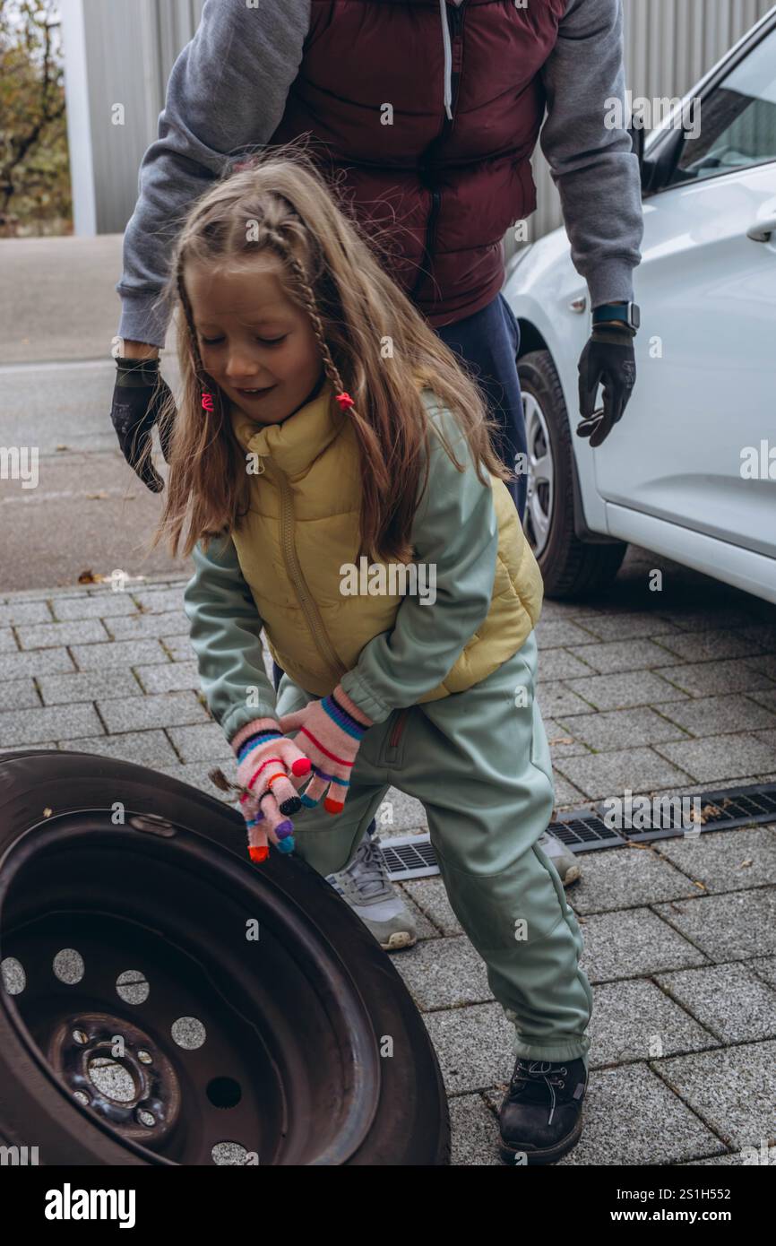 A little girl assists her father in changing the car tires,creating ...