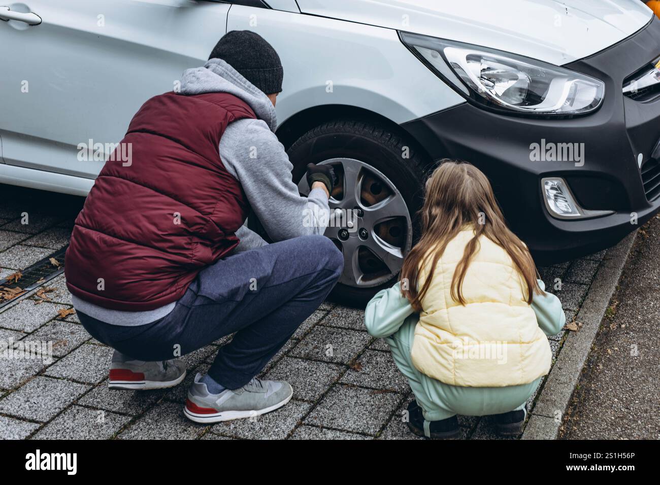 A little girl assists her father in changing the car tires,creating ...