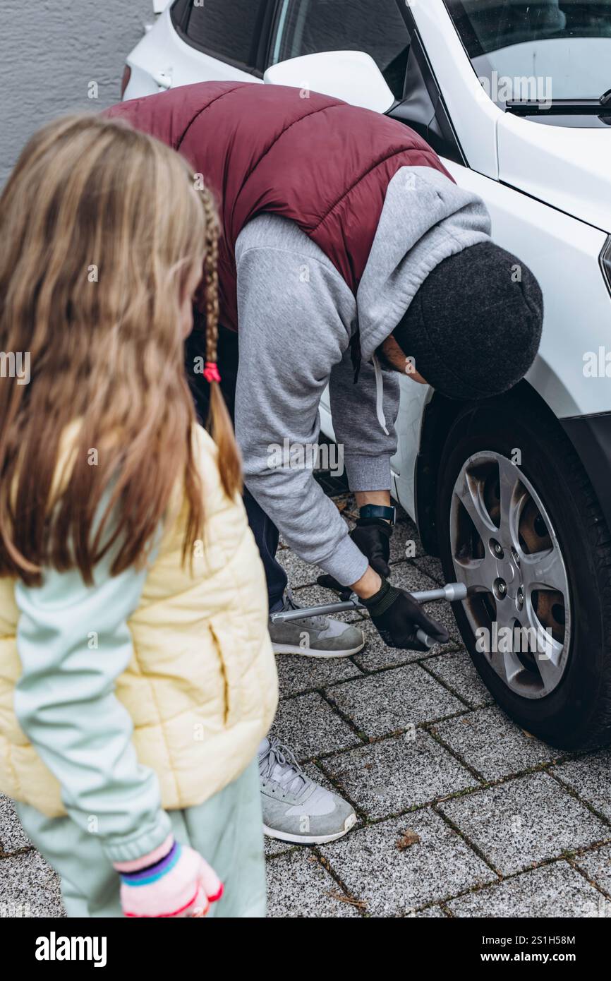 A little girl assists her father in changing the car tires,creating ...