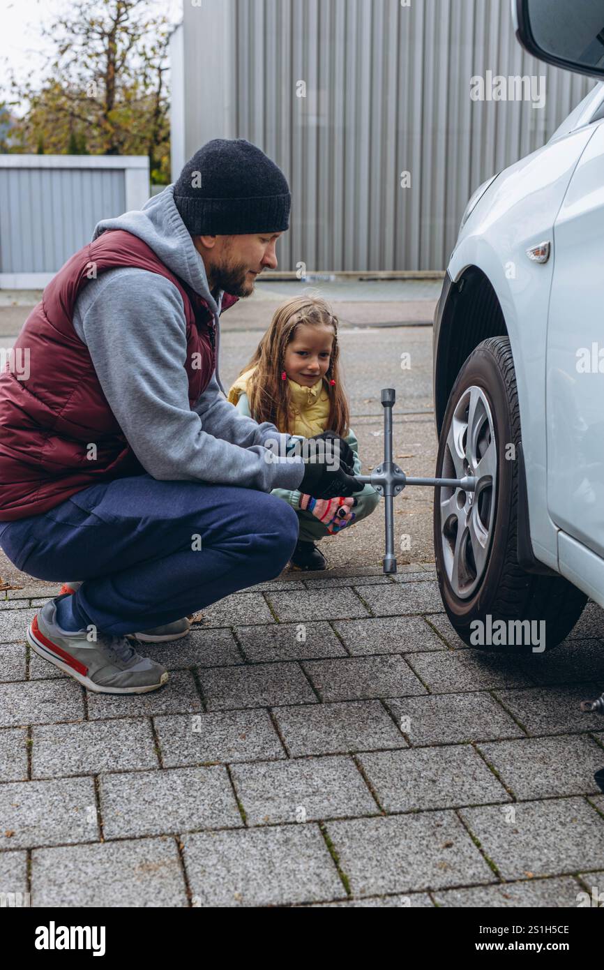 A little girl assists her father in changing the car tires,creating ...