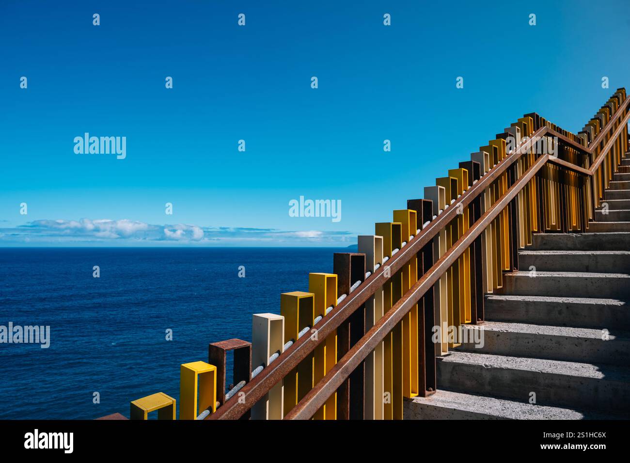 A staircase with yellow and brown railings leading to the ocean. The ...