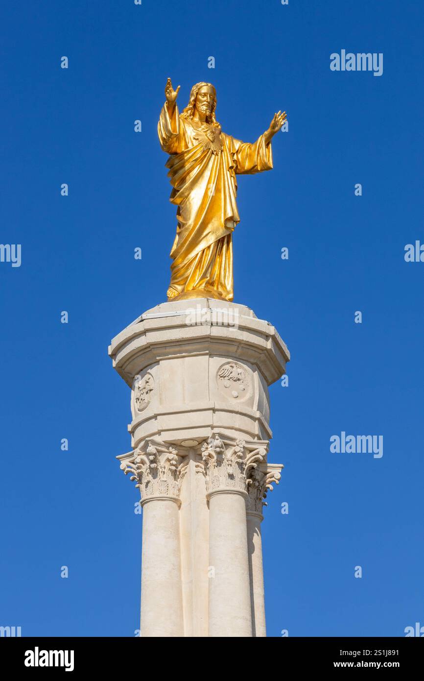 Golden Jesus Christ statue on a pillar against a clear blue sky. At the ...