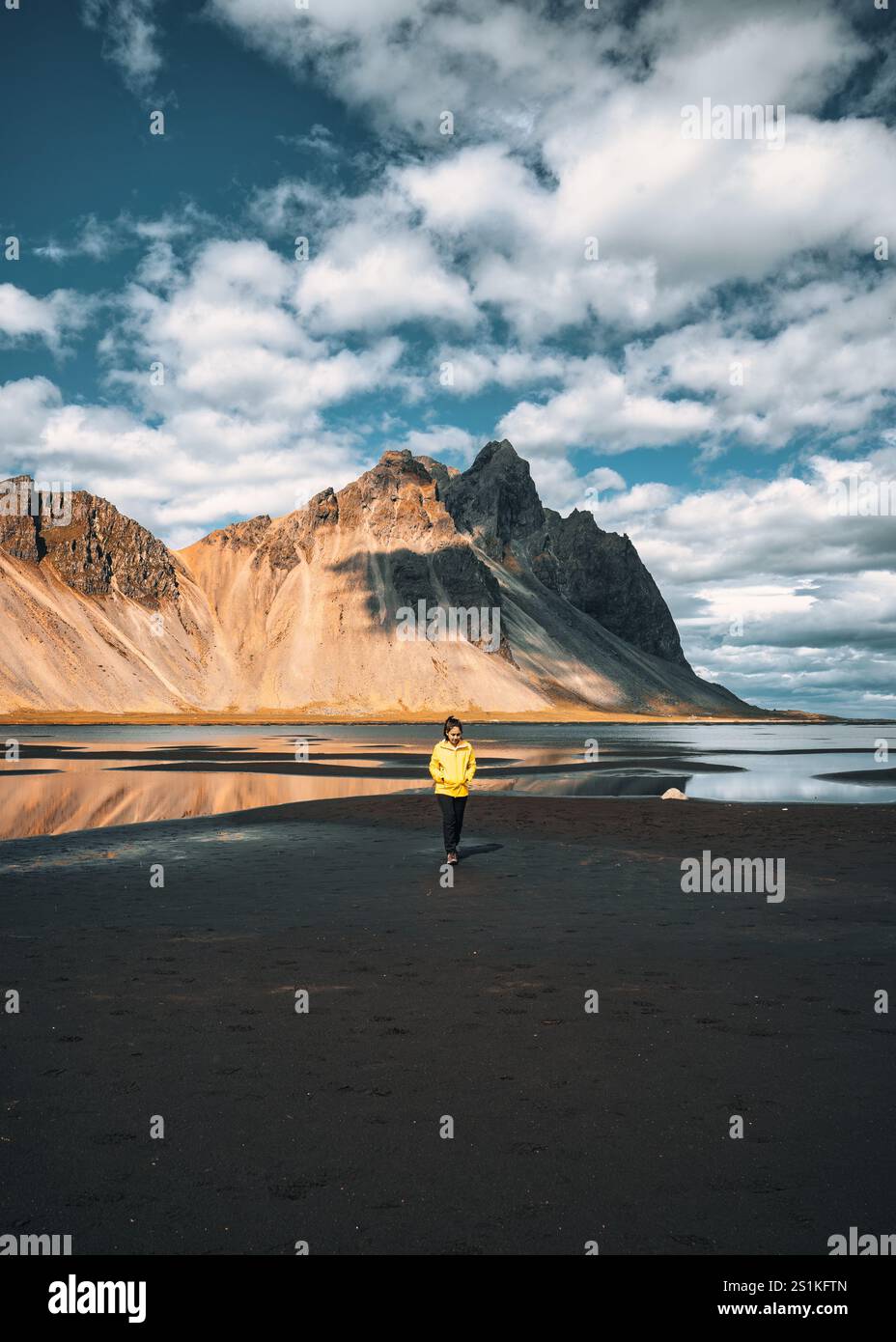 Asian woman in yellow jacket standing on black sand beach with majestic ...