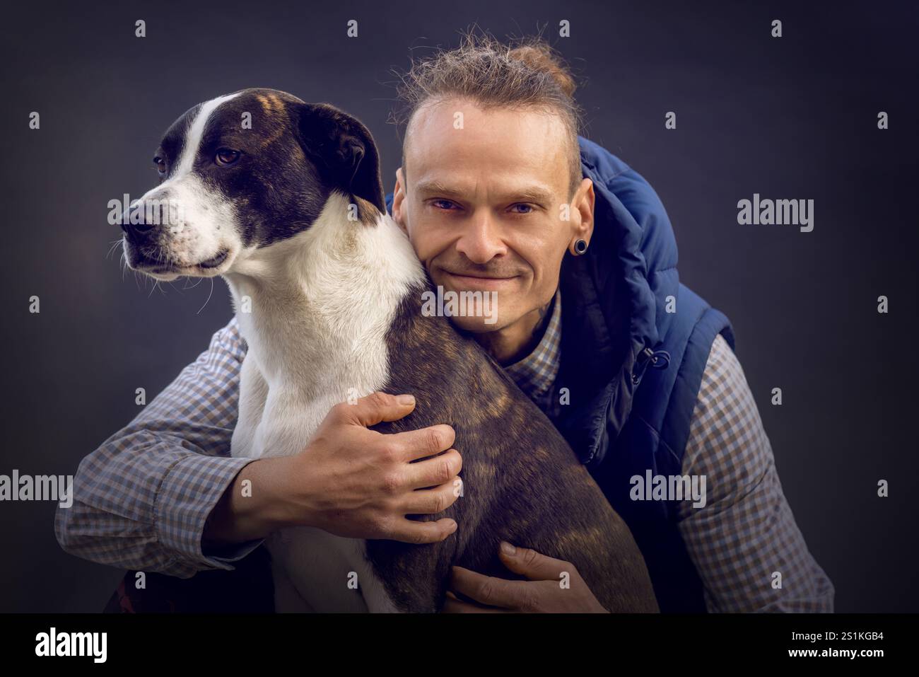 A man cuddle with his crossbreed dog in front of dark studio background ...