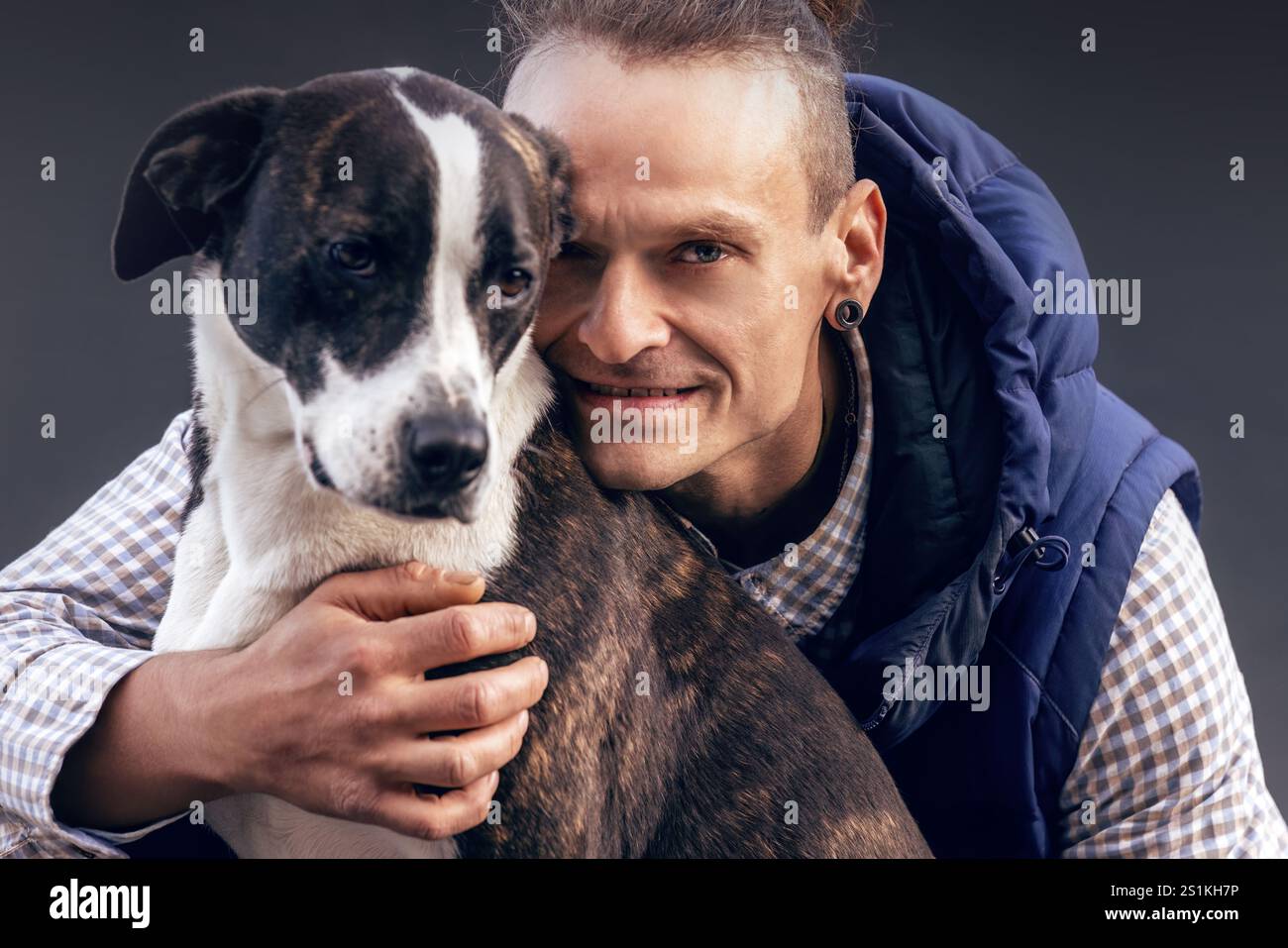 A man cuddle with his crossbreed dog in front of dark studio background ...