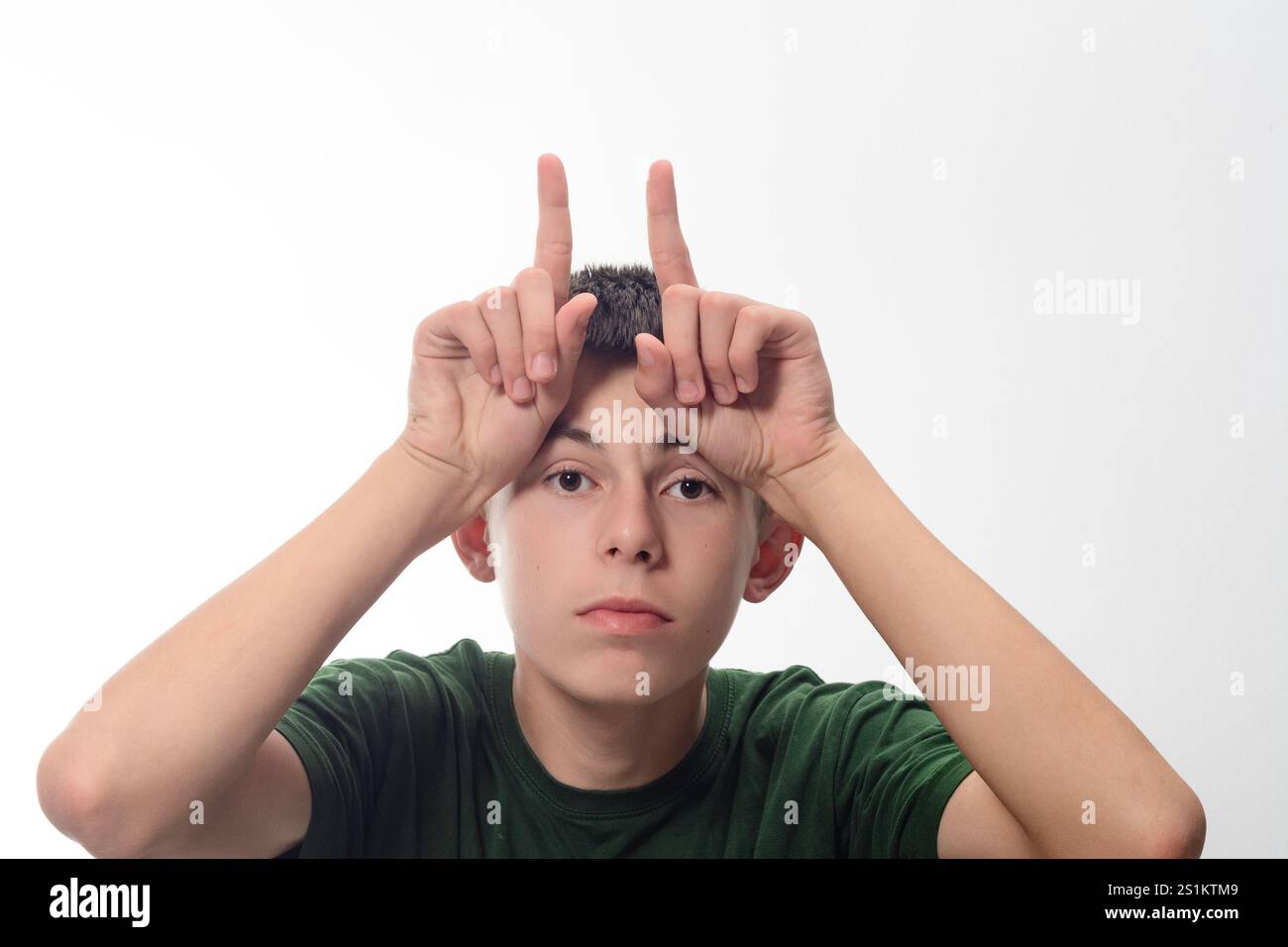 A portrait of a teenage boy playfully making horns on his forehead. He ...