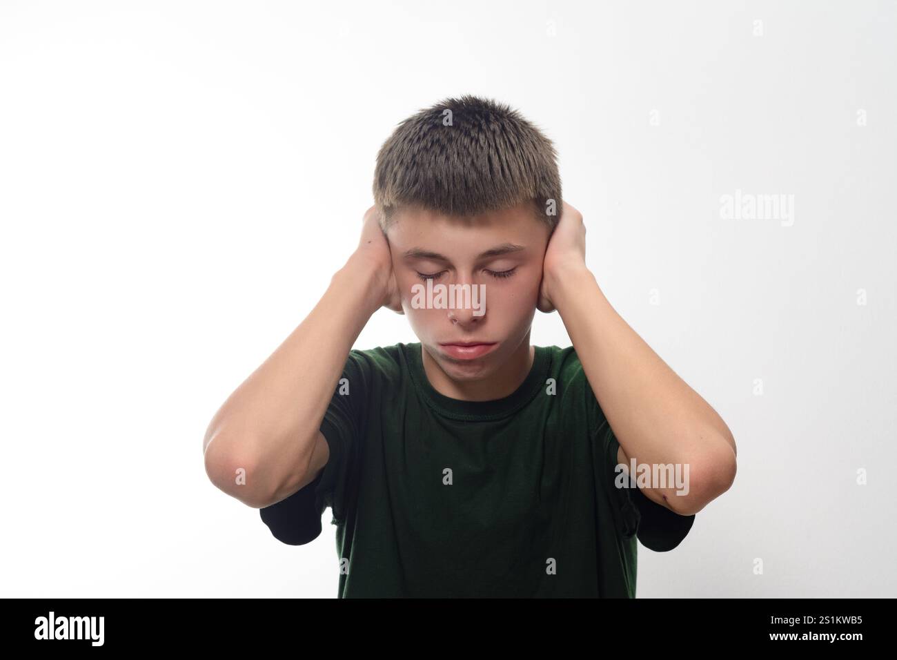 A young man with his eyes closed, hands over ears. He appears stressed ...
