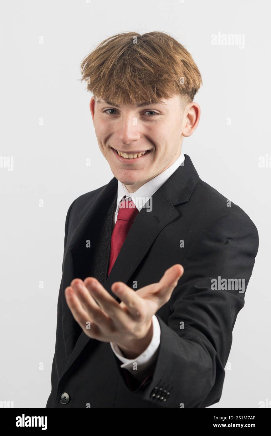 Happy Sixteen year old teenage boy wearing a suit gestures forward ...