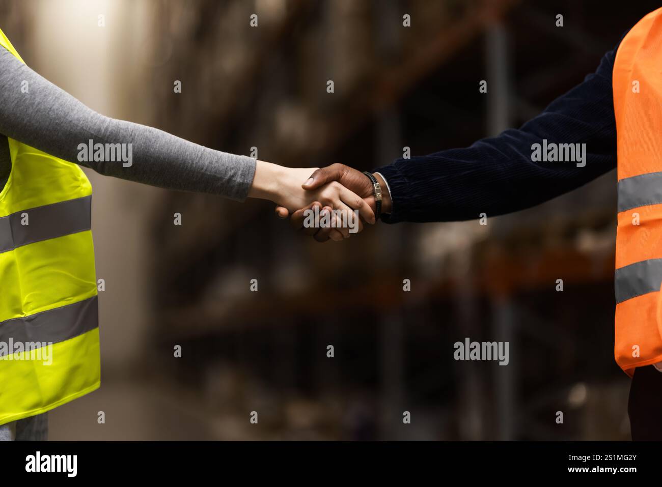 Close-up of two hands shaking in a warehouse setting. Workers wear high ...