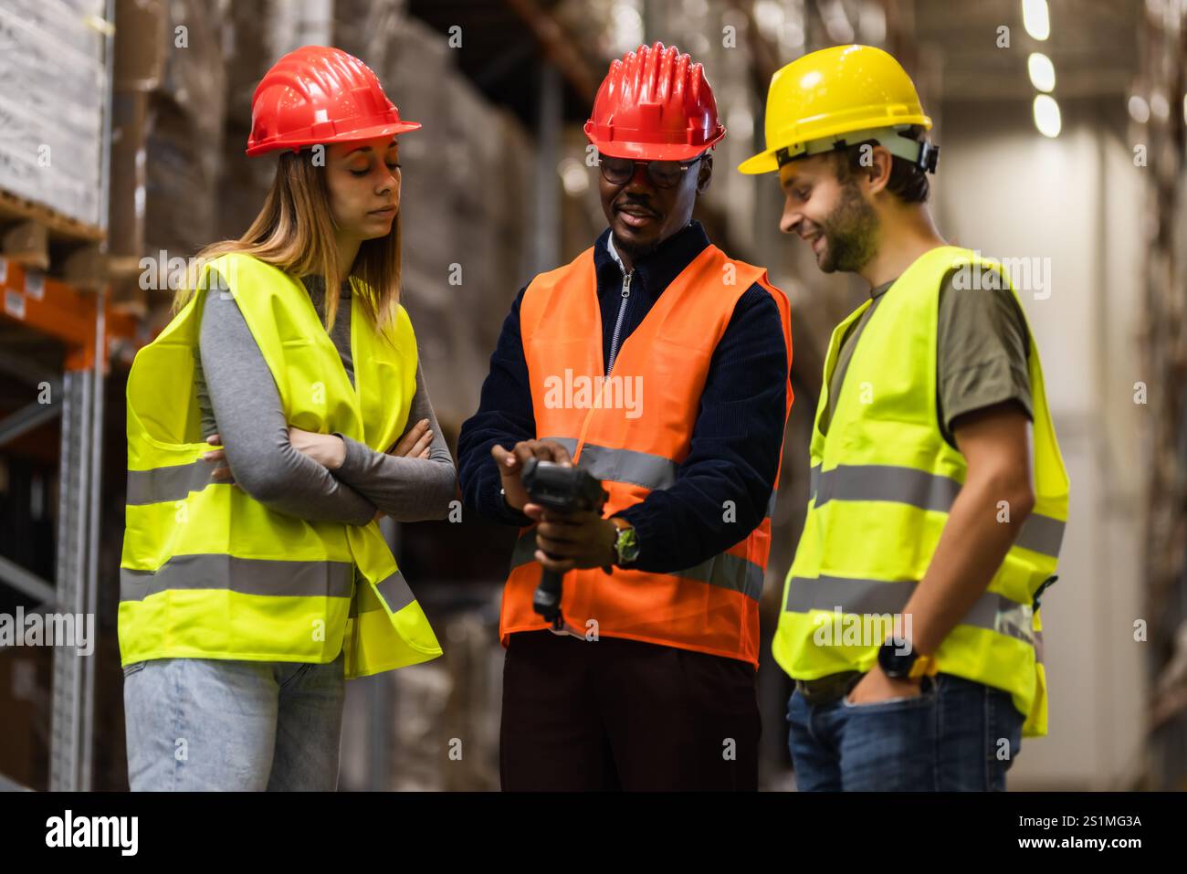 Three workers in a warehouse wearing safety gear engage in a logistics discussion, focusing on ...