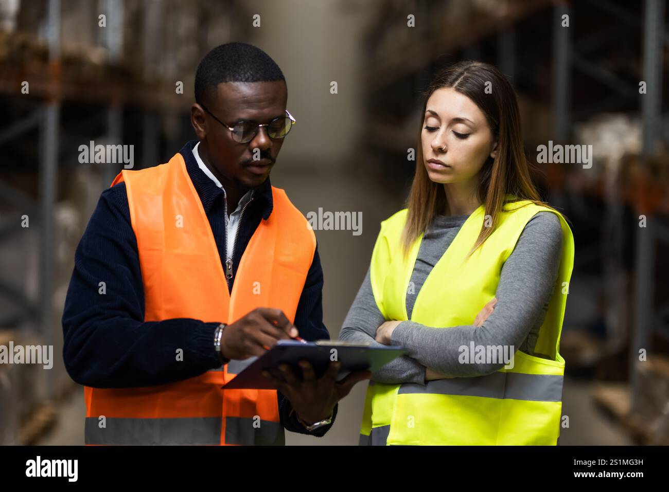 Two employees in a warehouse wearing orange and yellow safety vests ...