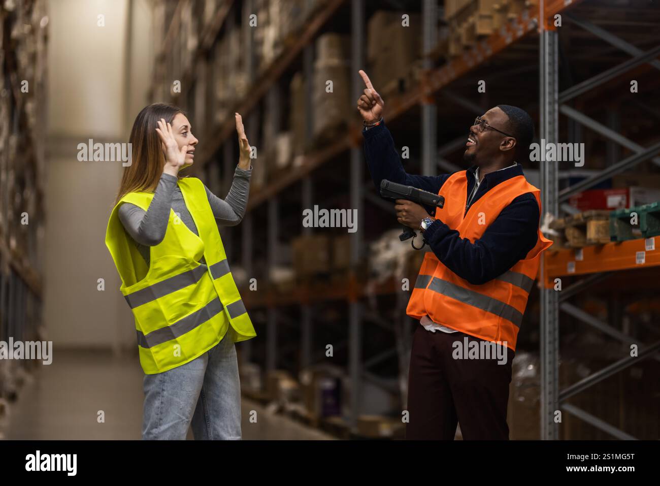 Two workers in a warehouse communicate effectively, wearing high-visibility vests, surrounded by ...
