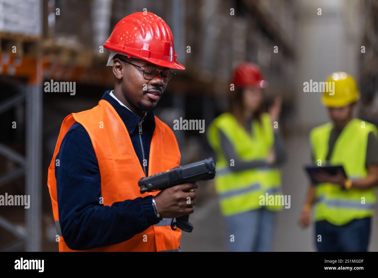 A warehouse worker in a safety vest and helmet uses a barcode scanner ...