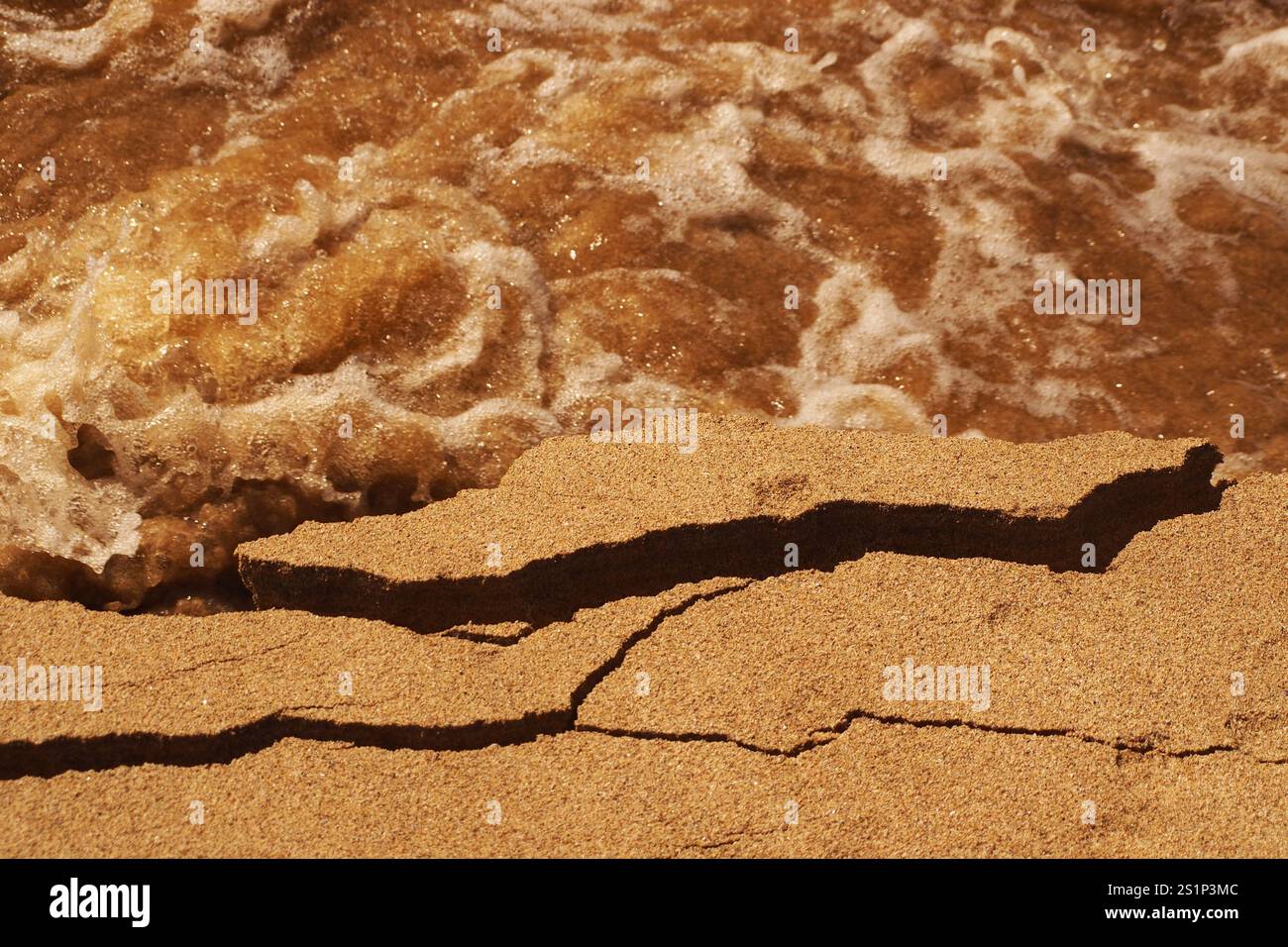 Erosion of sand at the edge of a sandy beach where a river flows into ...