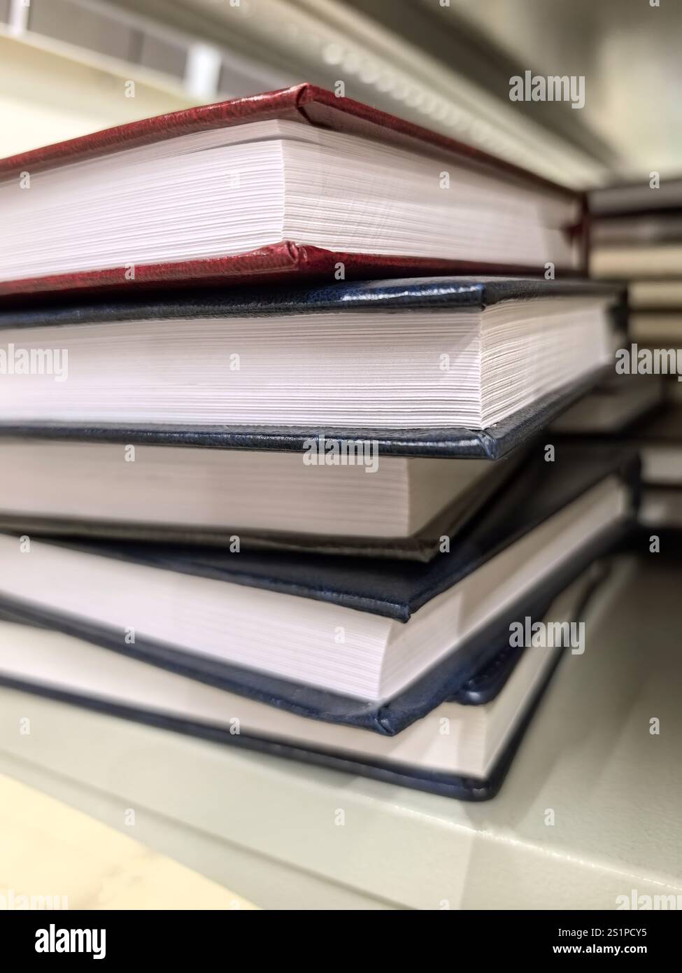 A collection of various hardcover books is neatly stacked on a shelf ...