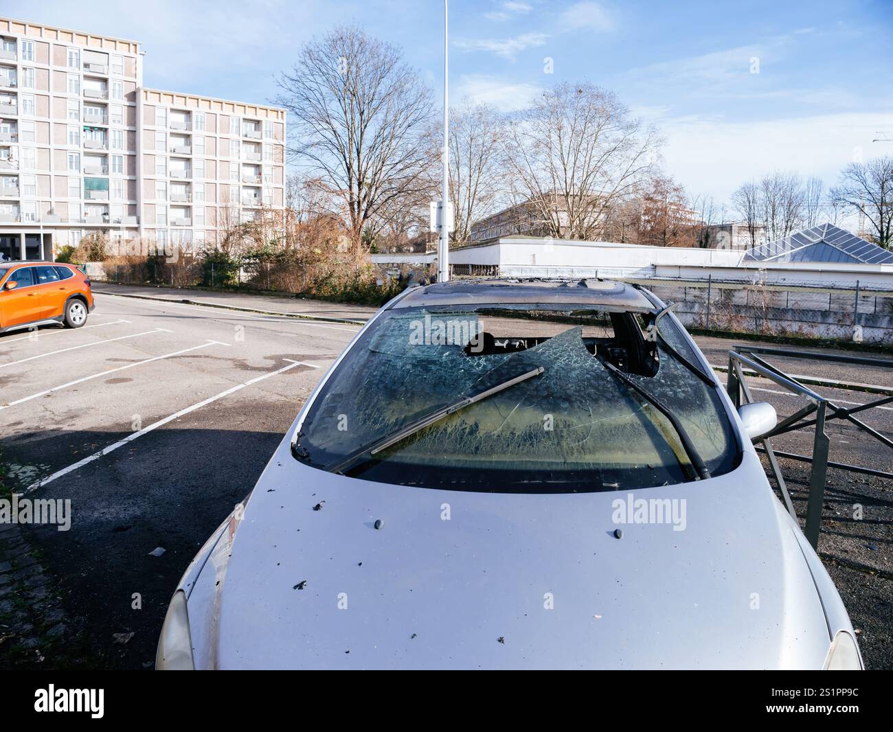 A burned-out car with shattered windows in a parking lot, set against ...