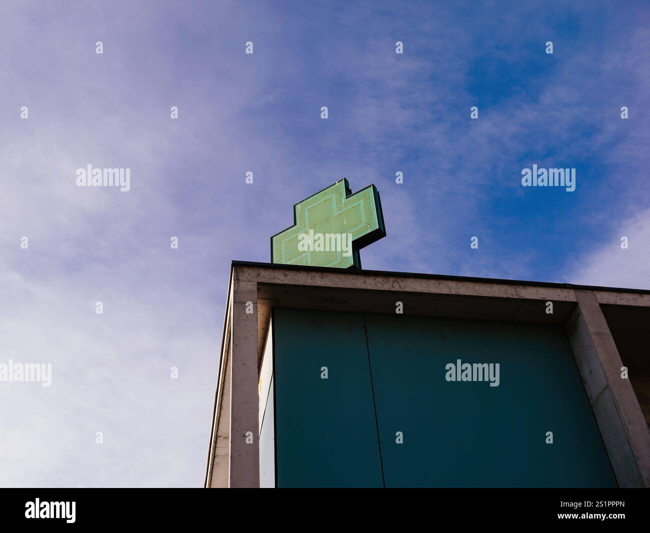 A green illuminated pharmacy cross sign mounted on the corner of a ...