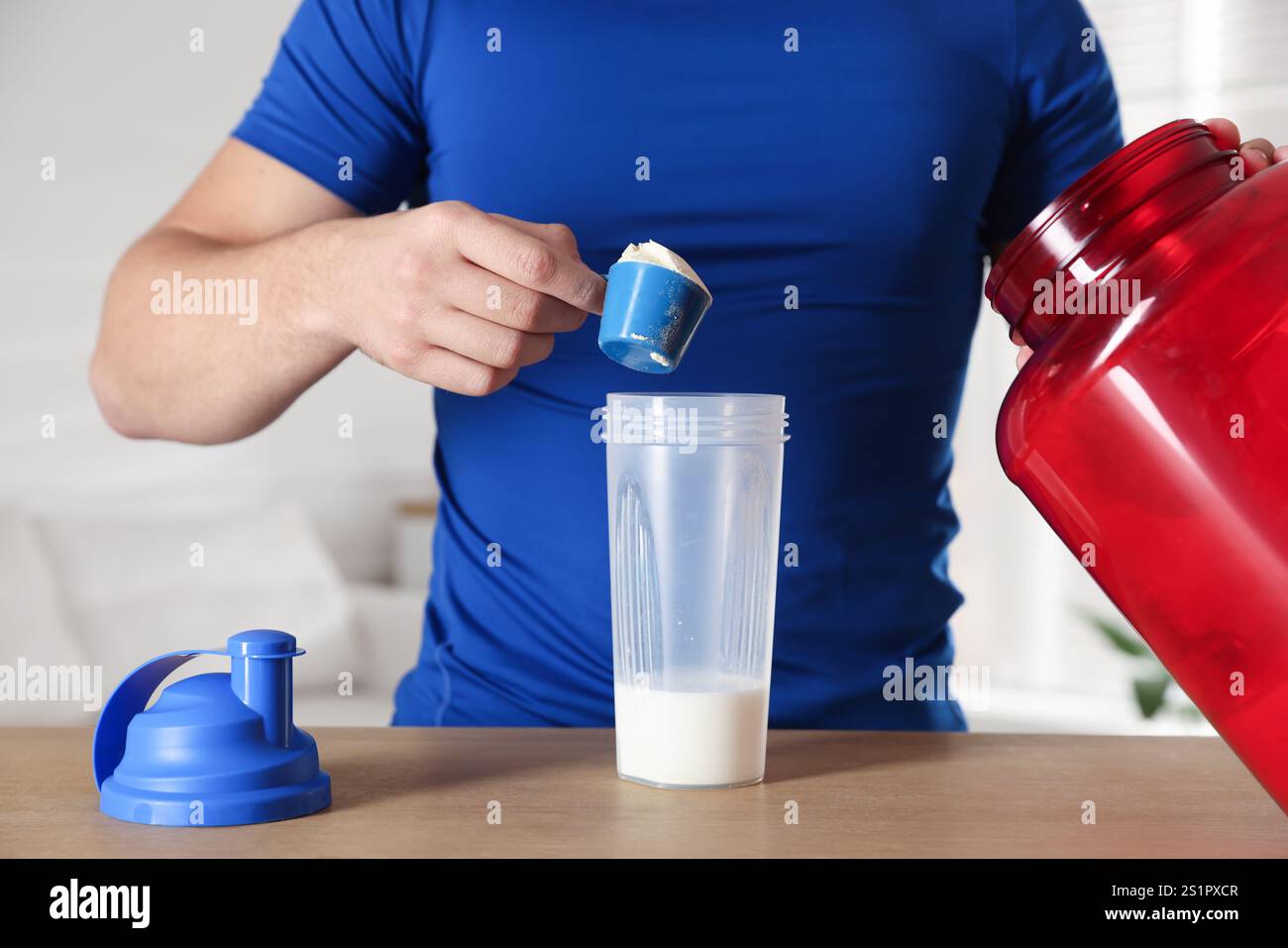Making protein cocktail. Man adding powder into shaker at wooden table ...