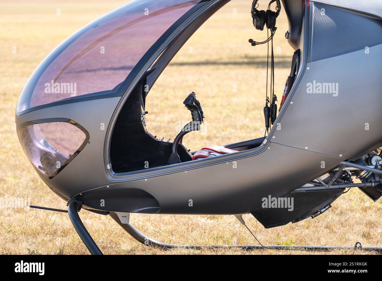 Modern gray two-seater small helicopter with open doors on a grassy ...