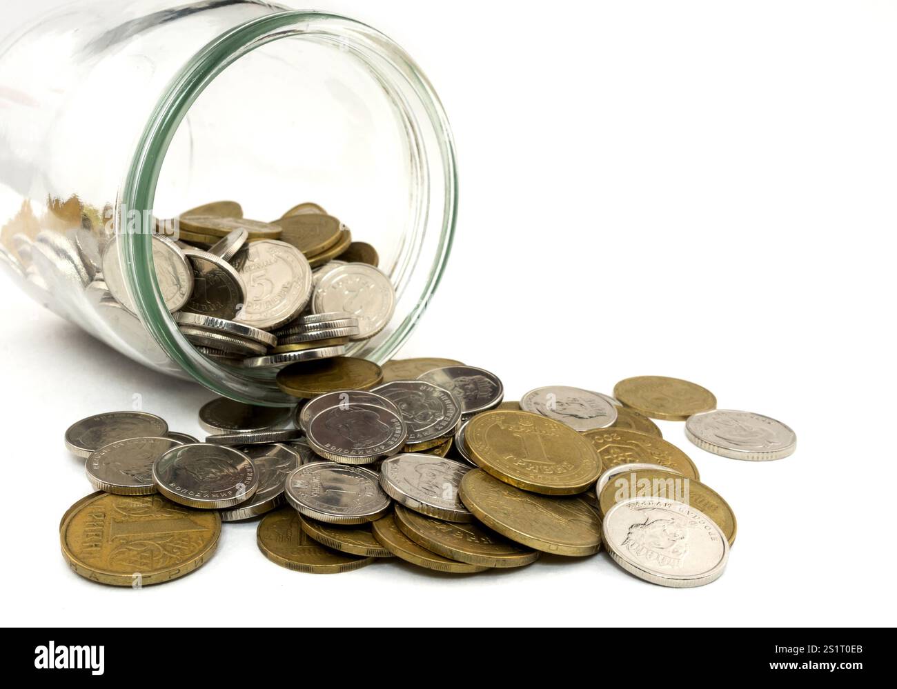 A glass jar lies on its side, spilling out a mix of various coins onto ...