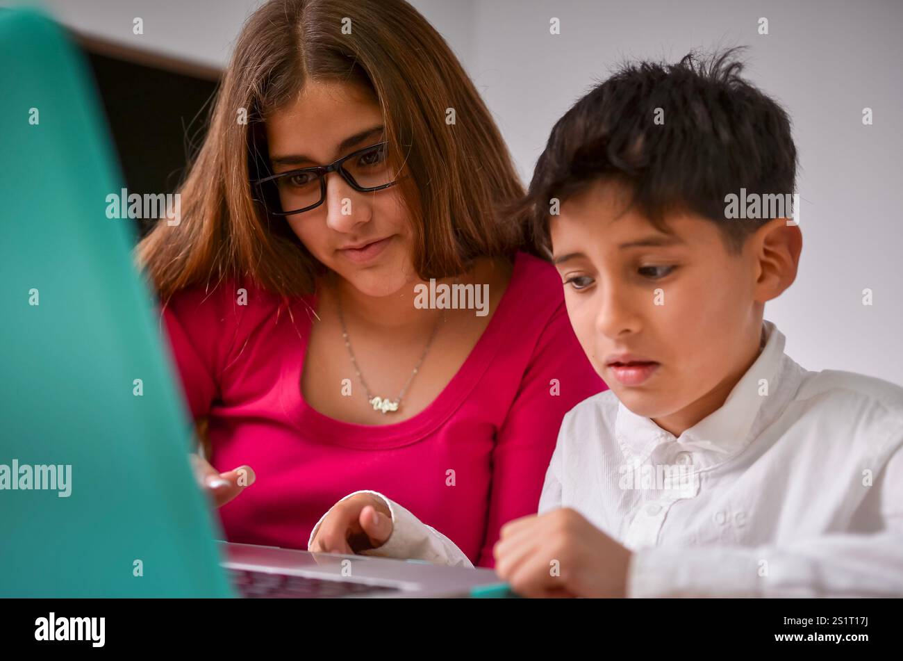 Teenager girl helping her younger brother studying and doing homework using a laptop computer ...