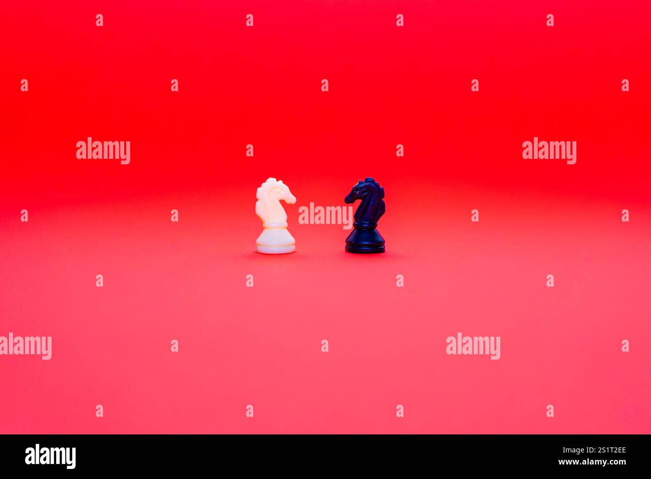 A white chess knight faces a black chess knight on a bright red surface ...