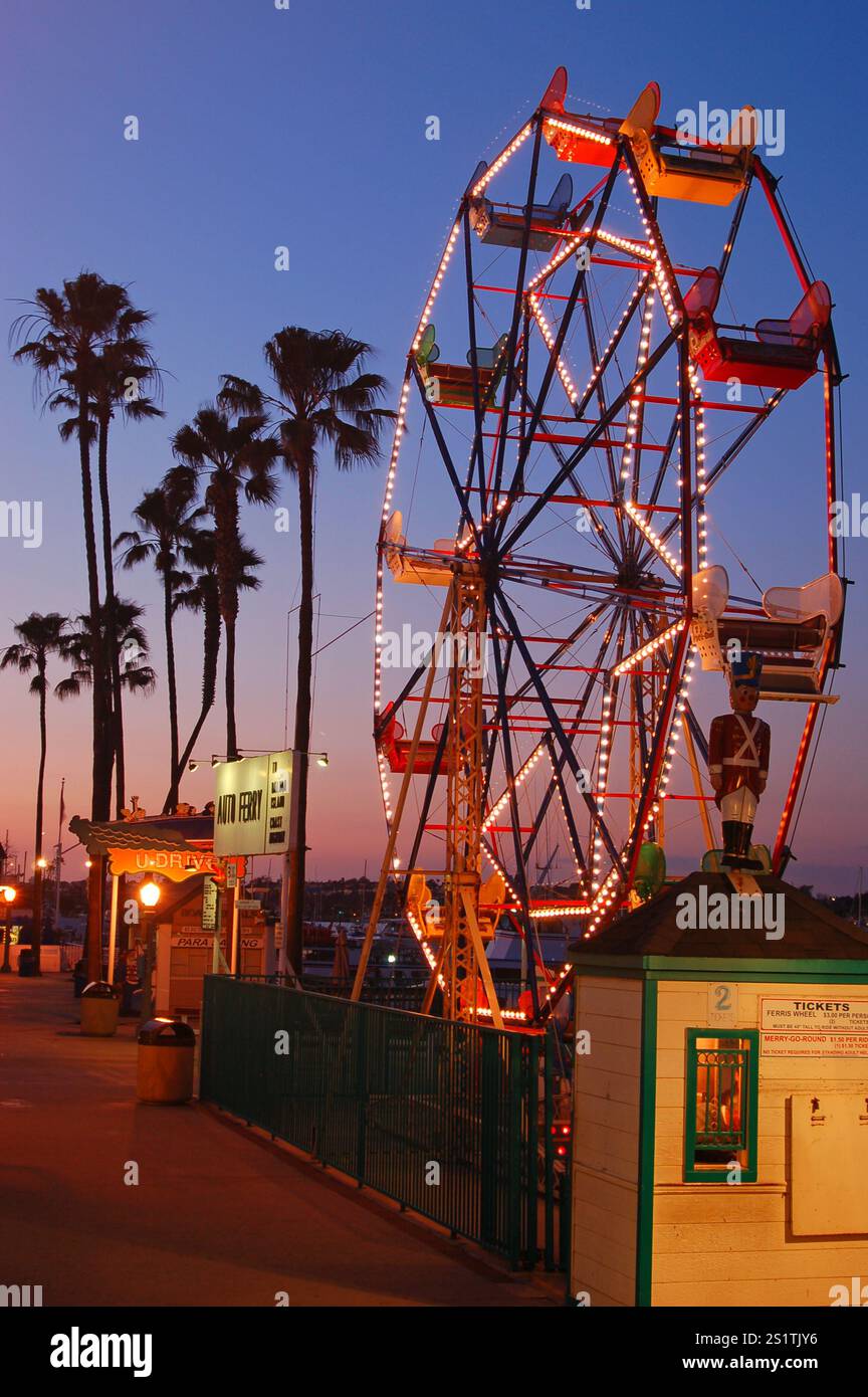 A small Ferris wheel is illuminated at dusk at an amusement park area ...