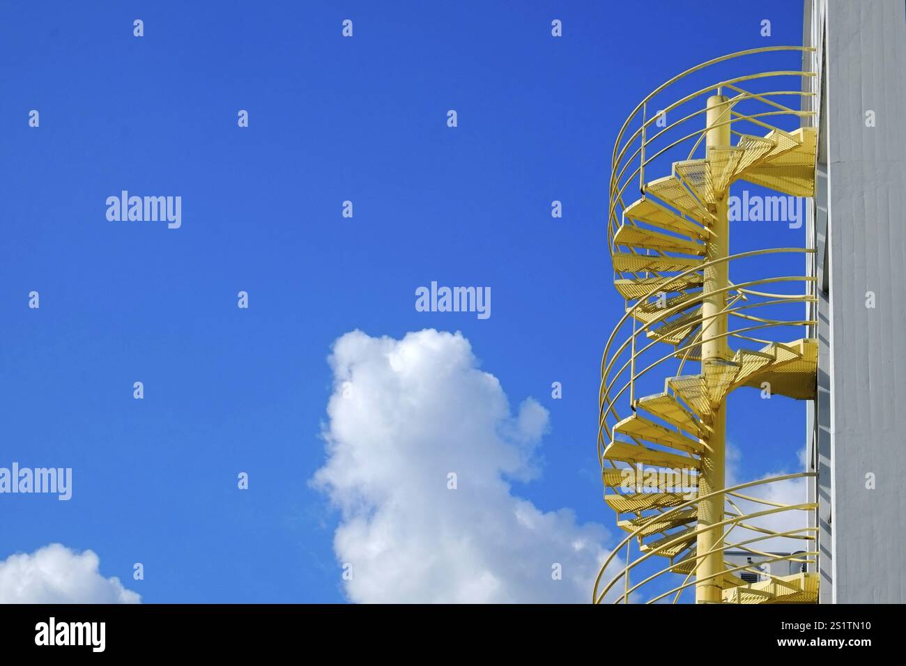 Bright yellow painted outside spiral staircase in front of a steel blue ...