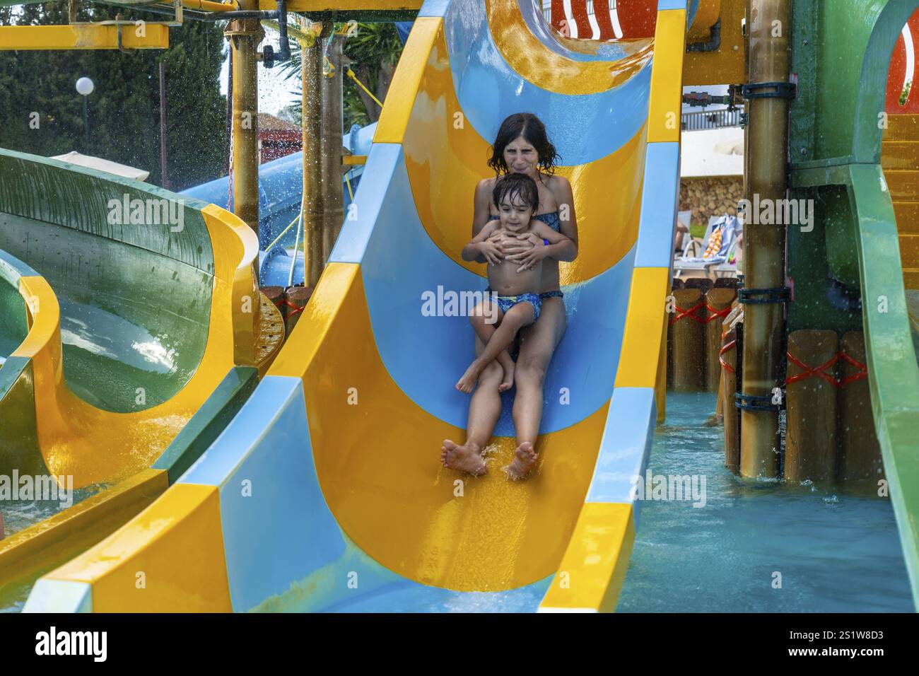 A woman and a child are sliding down a water slide. The slide is yellow ...