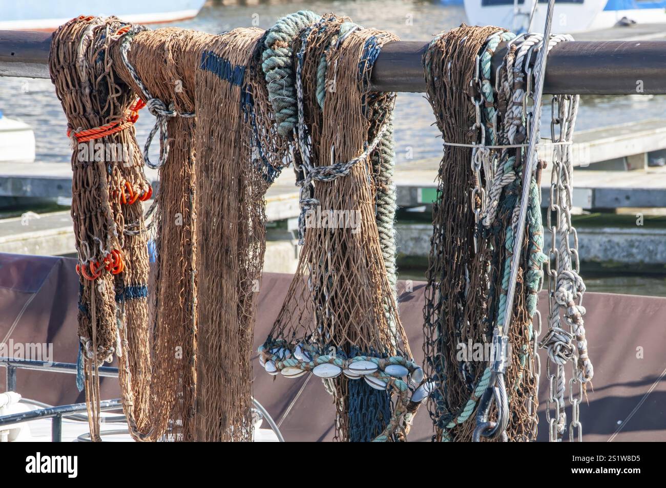 Brown fishing nets with floats and chains are hanging on a railing to ...